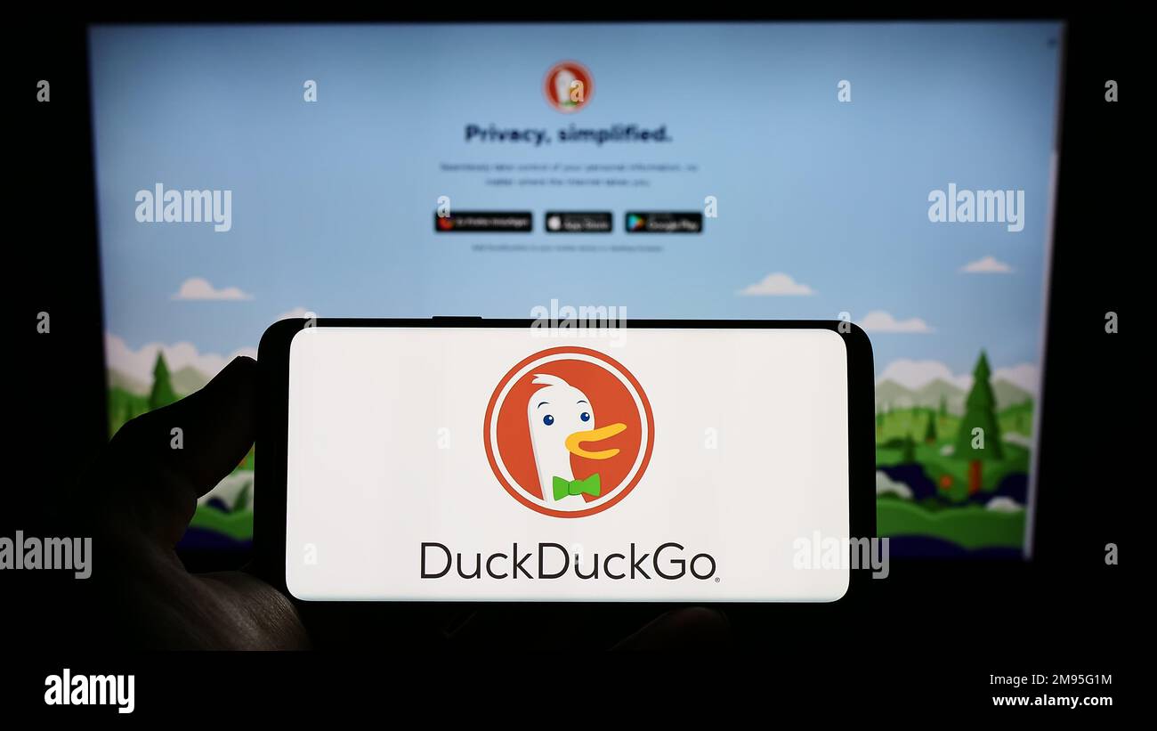 Person holding mobile phone with logo of Internet search engine DuckDuckGo (DDG) on screen in ...