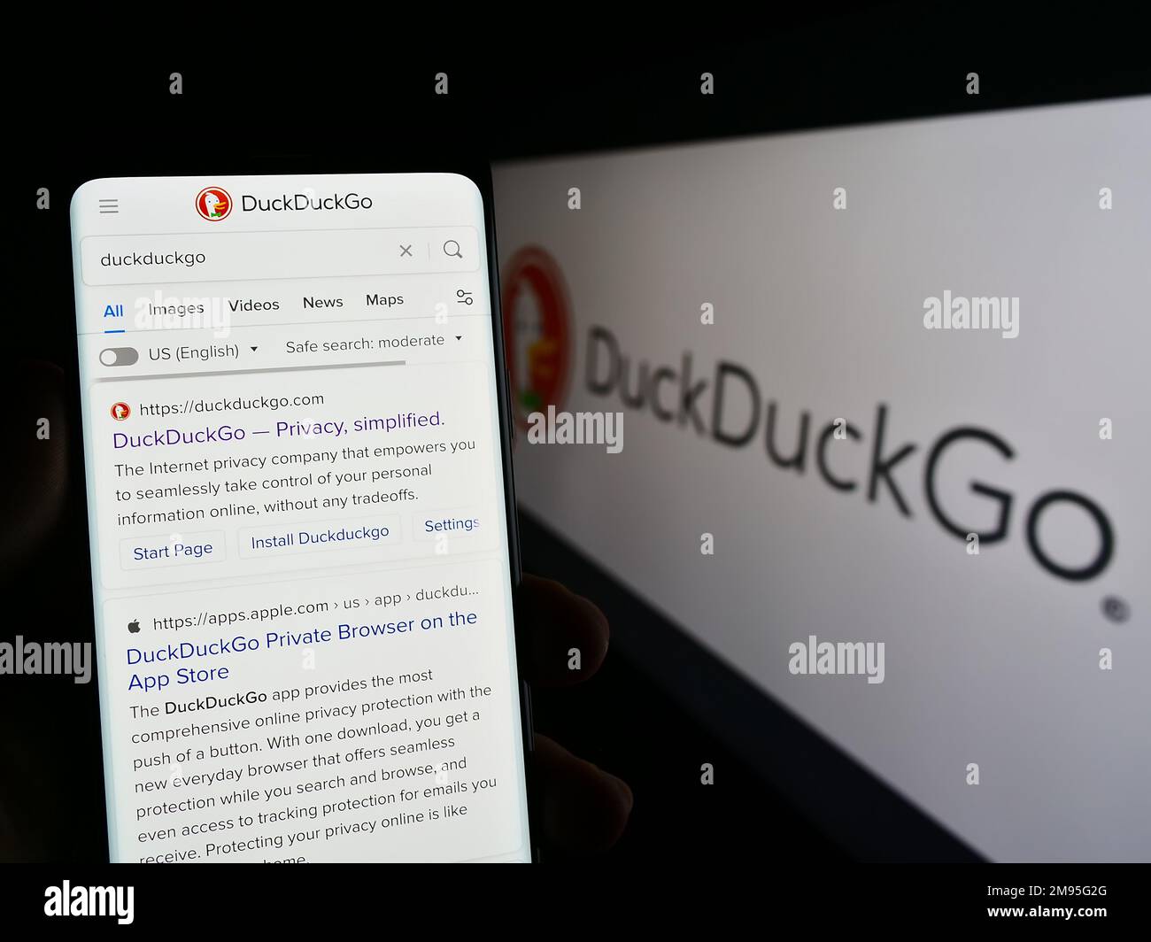 Person holding cellphone with webpage of Internet search engine DuckDuckGo (DDG) on screen in ...