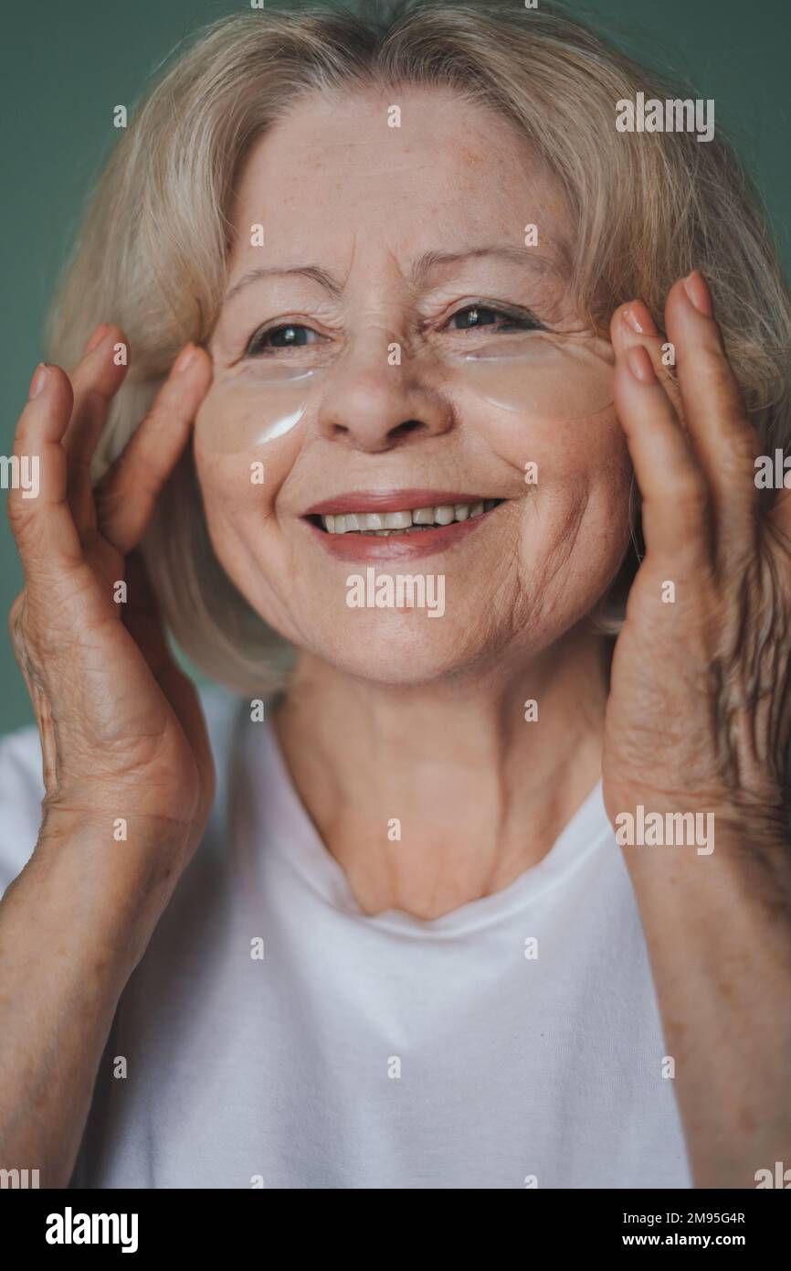 Portrait of smiling woman applying eye patches on her face while ...