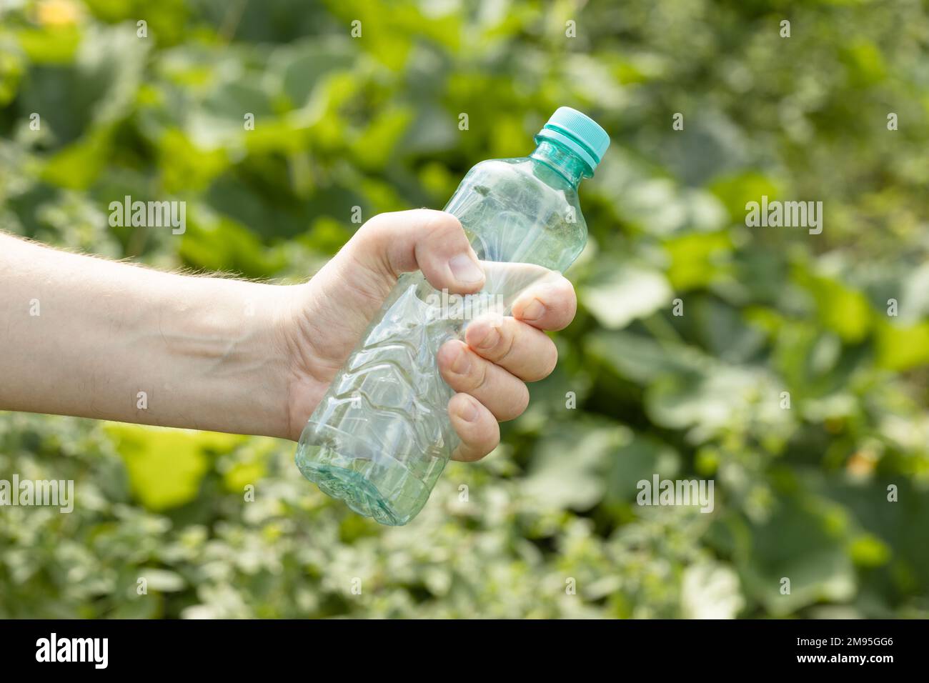 Hand holding crumpled empty plastic bottle in the park Stock Photo - Alamy