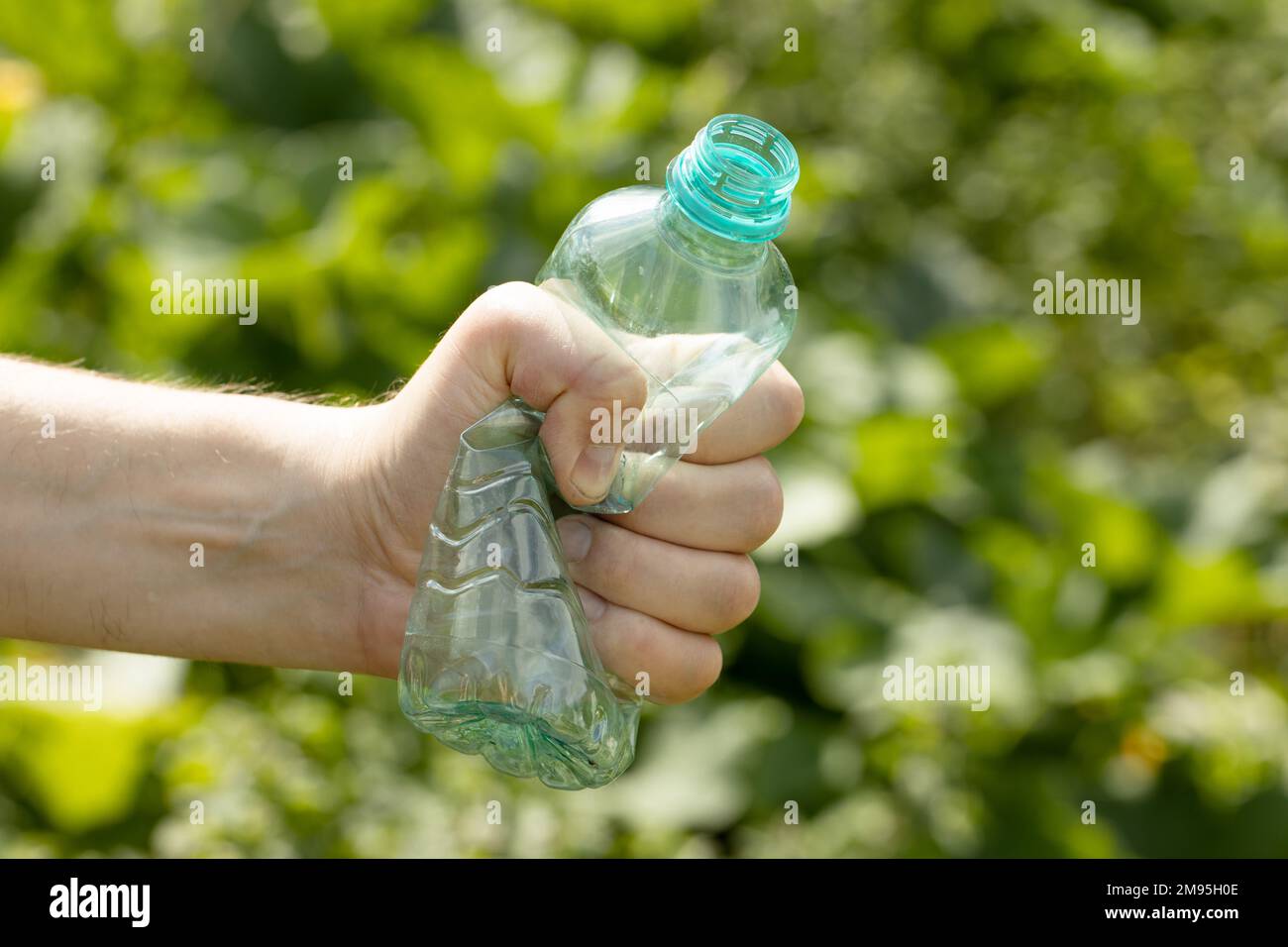 Hand holding crumpled empty plastic bottle in the park Stock Photo - Alamy