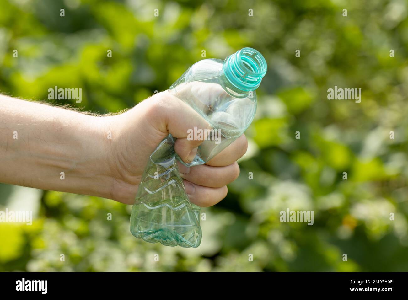 Hand holding crumpled empty plastic bottle in the park Stock Photo - Alamy