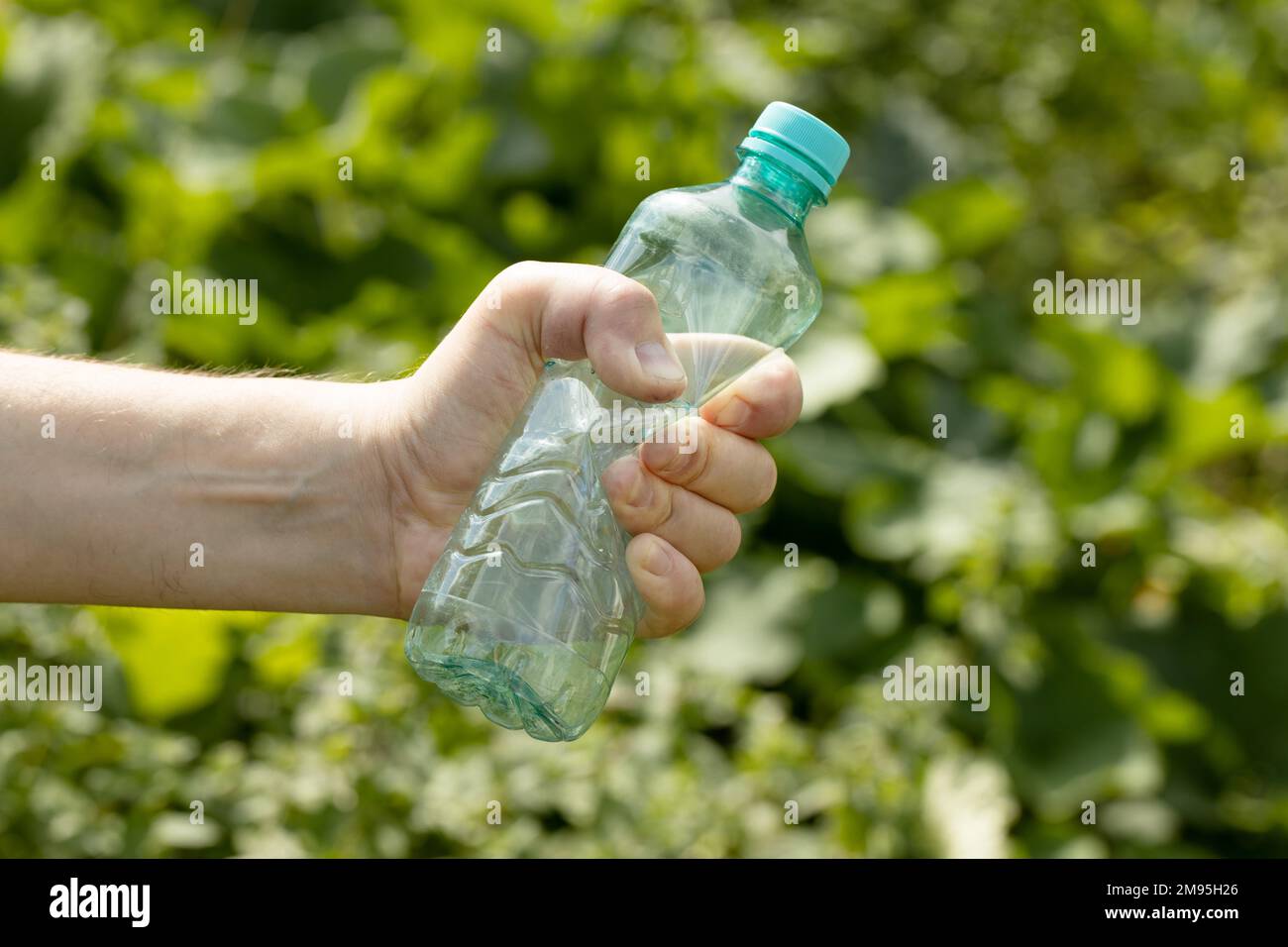 Hand holding crumpled empty plastic bottle in the park Stock Photo - Alamy