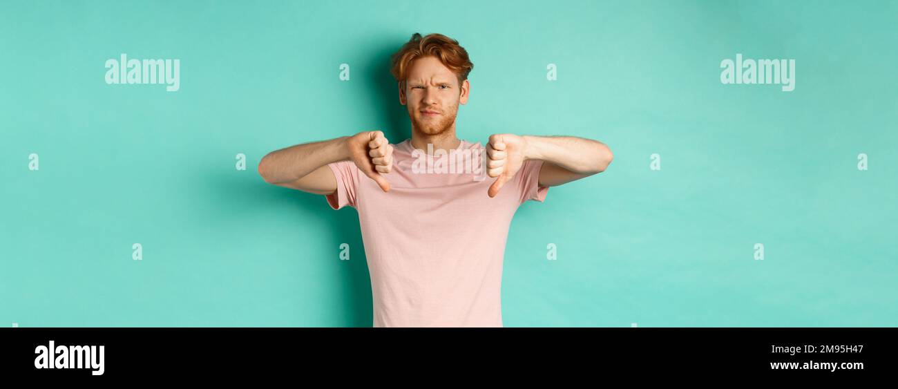 Disappointed guy with red hair showing thumbs-down, frowning and ...