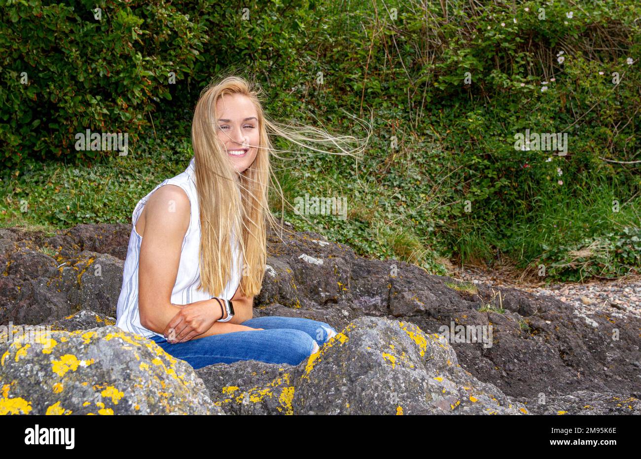 Rhianna Martin, a beautiful blonde woman, sits on rocks while having ...