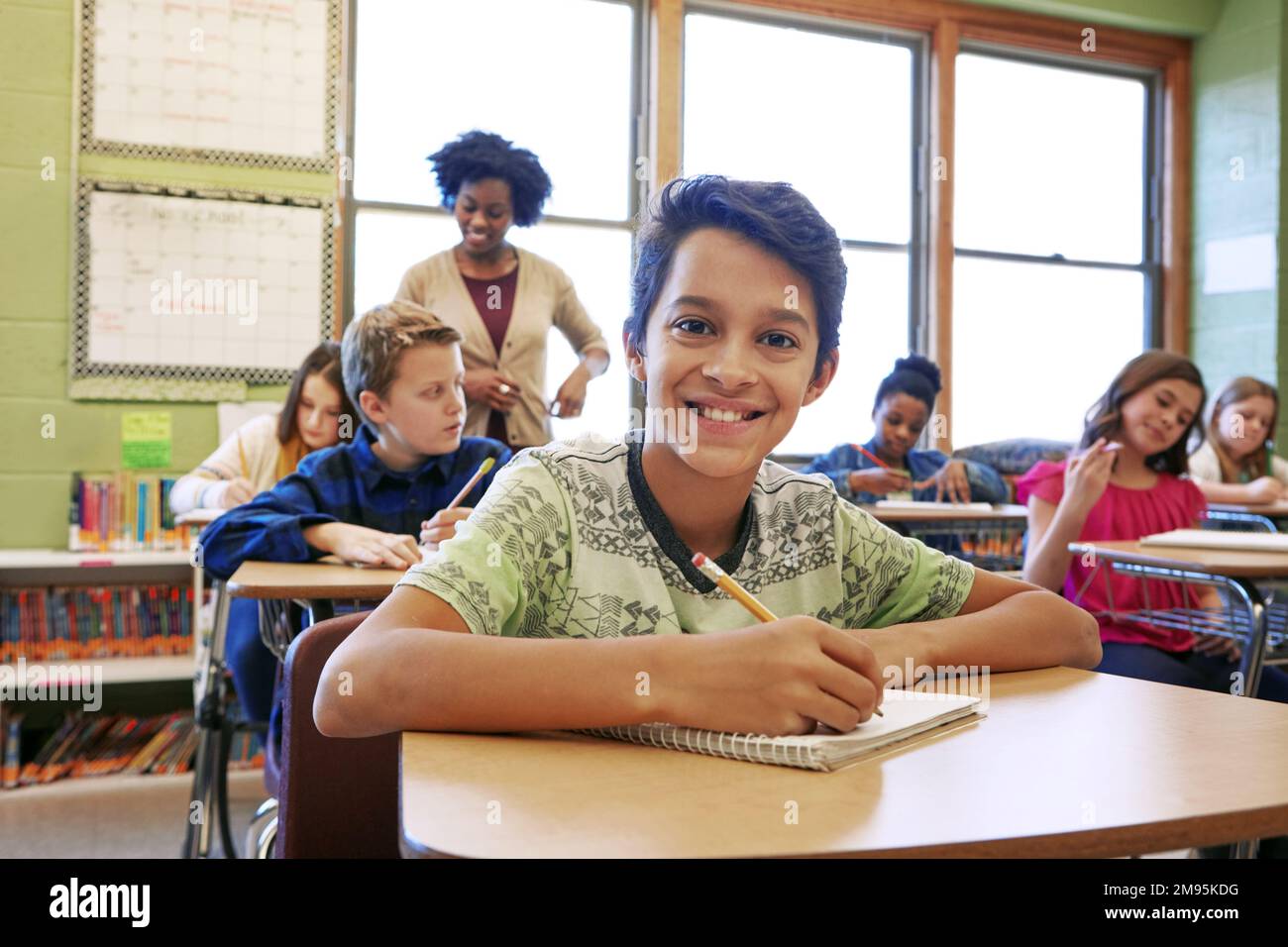 Happy, education portrait or kid in classroom writing in notebook for ...