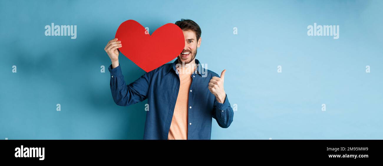 Happy man showing valentines heart and thumbs-up gesture, standing over ...