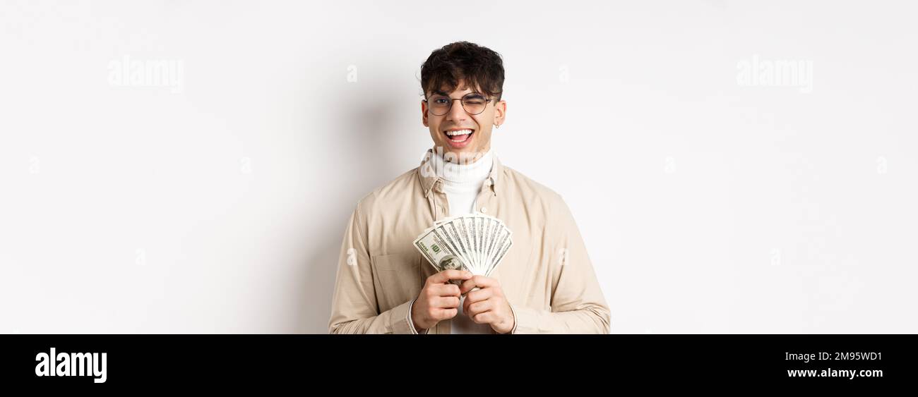 Handsome young man winking and showing dollar bills, holding fan of ...