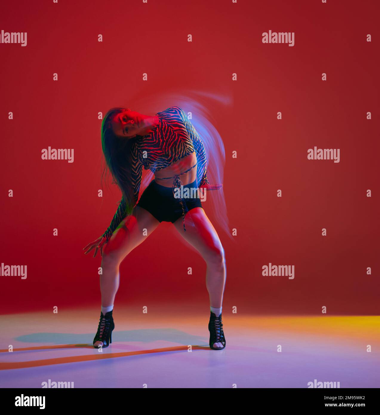 Portrait of young girl dancing heels dance over red background in neon ...