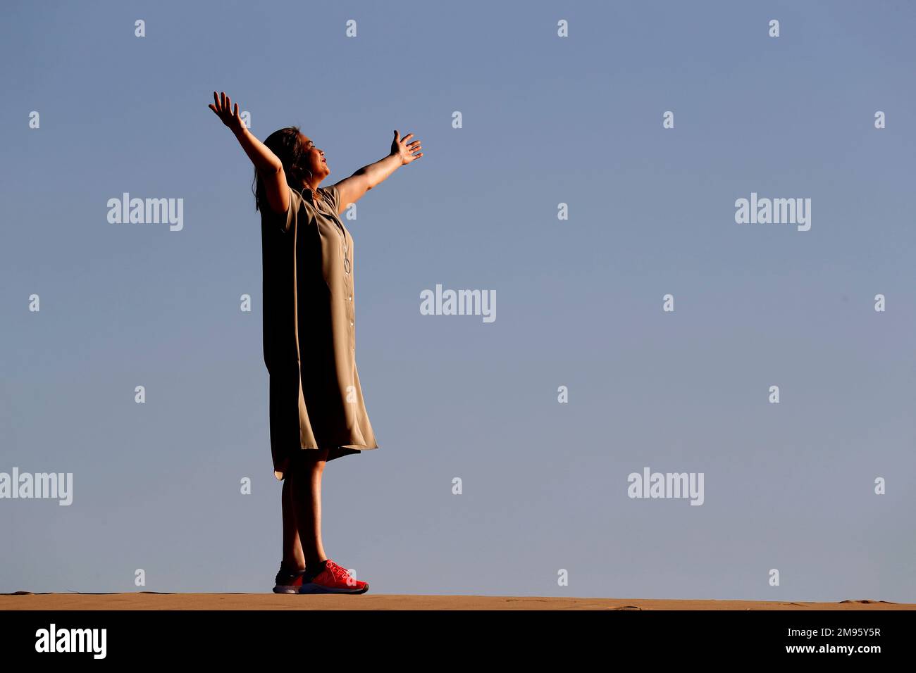 Woman with arms outstretched walking on sand dune in the desert ...