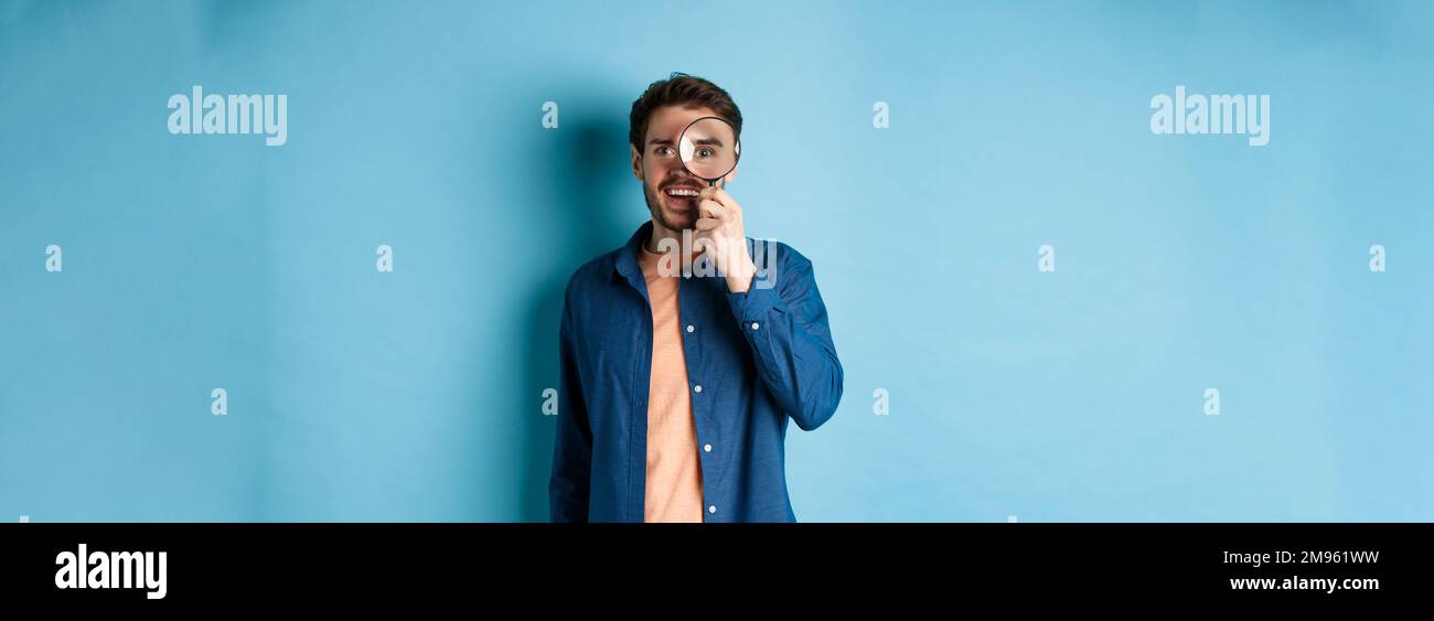 Cheerful young man found something good, smiling and looking through ...