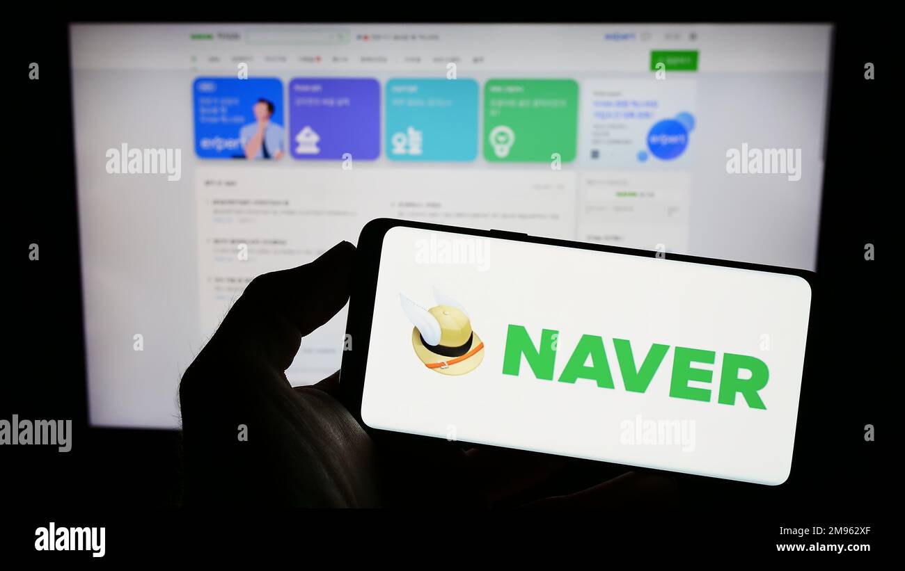 Person holding cellphone with logo of search engine company Naver Corporation on screen in front ...