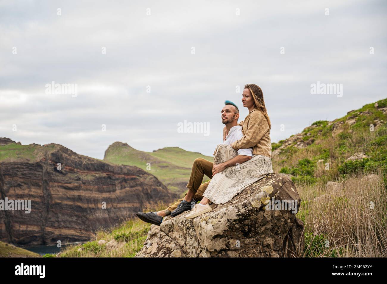A young couple sits on a rock surrounded by hills and rocks in the ...