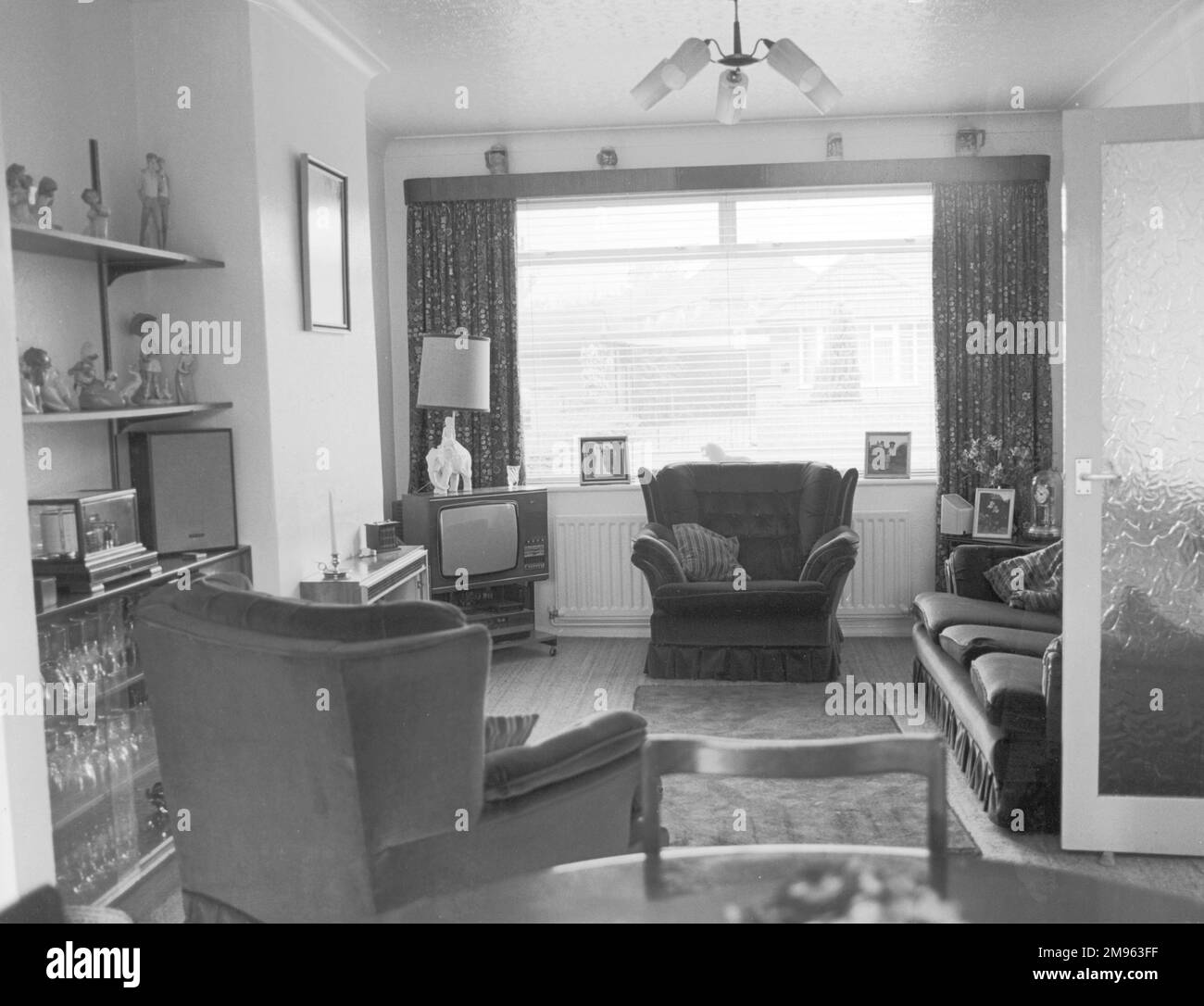 Typical suburban lounge with ornaments on shelves, family photographs ...