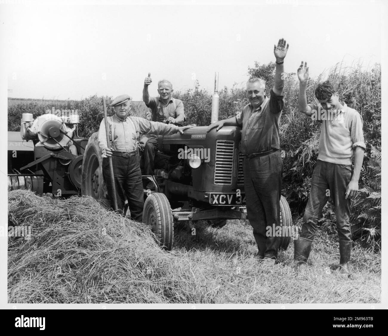 A group of happy farmworkers gather round a tractor Stock Photo - Alamy