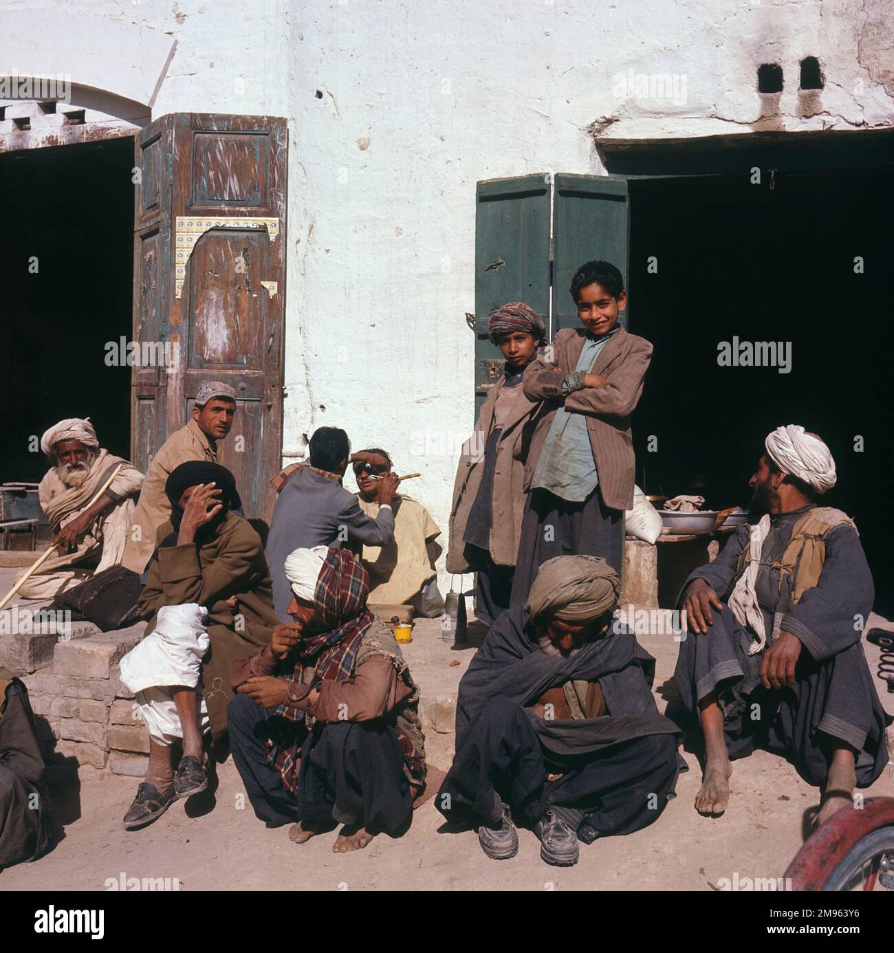 A group of men and boys (including a barber shaving a client) in front ...
