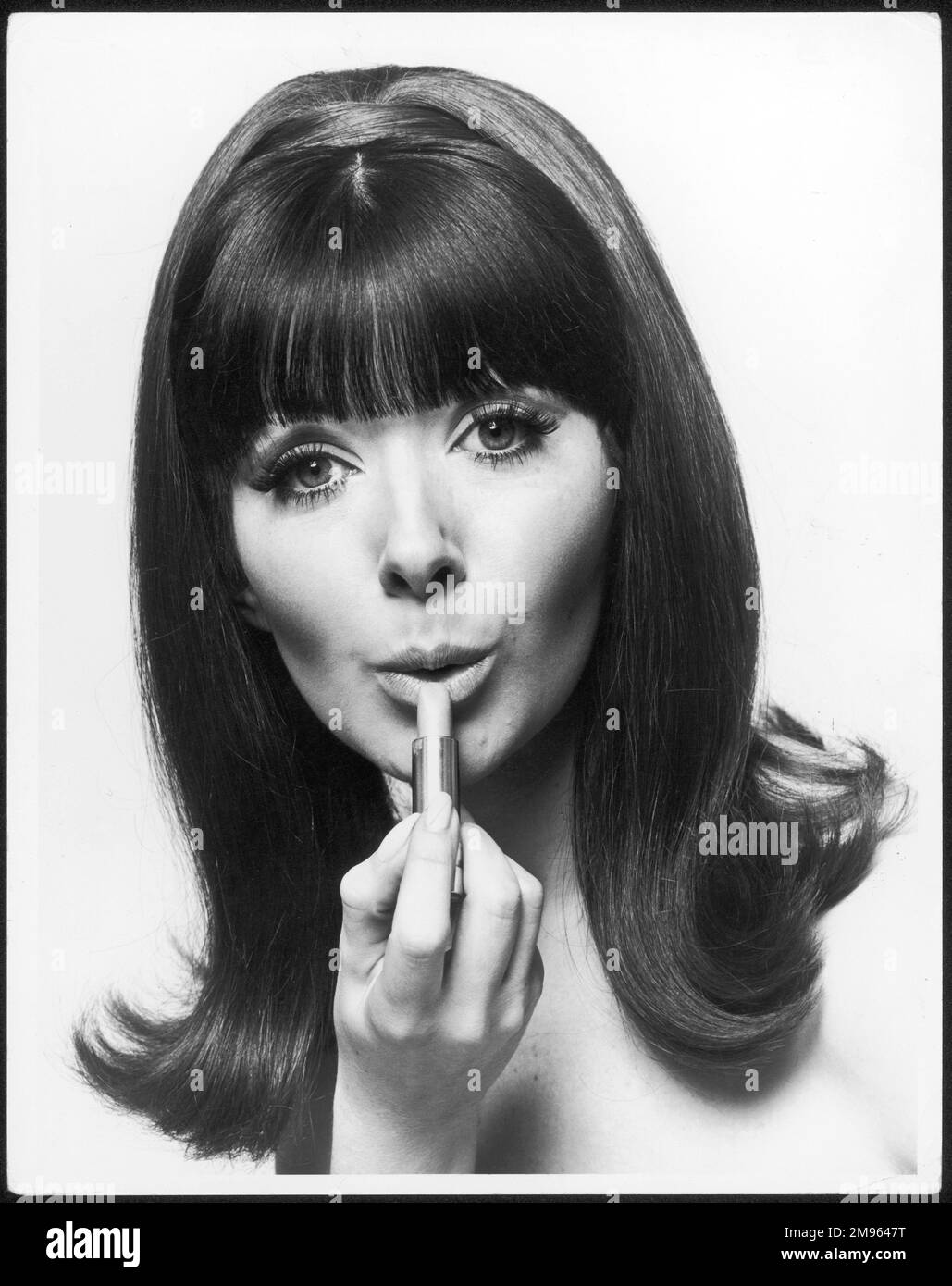 A model with long, straight dark hair, pouts as she applies her pearly ...