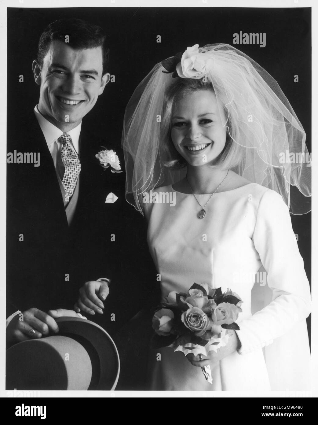 Newlyweds pose for the camera, the bride holding her bouquet of roses ...