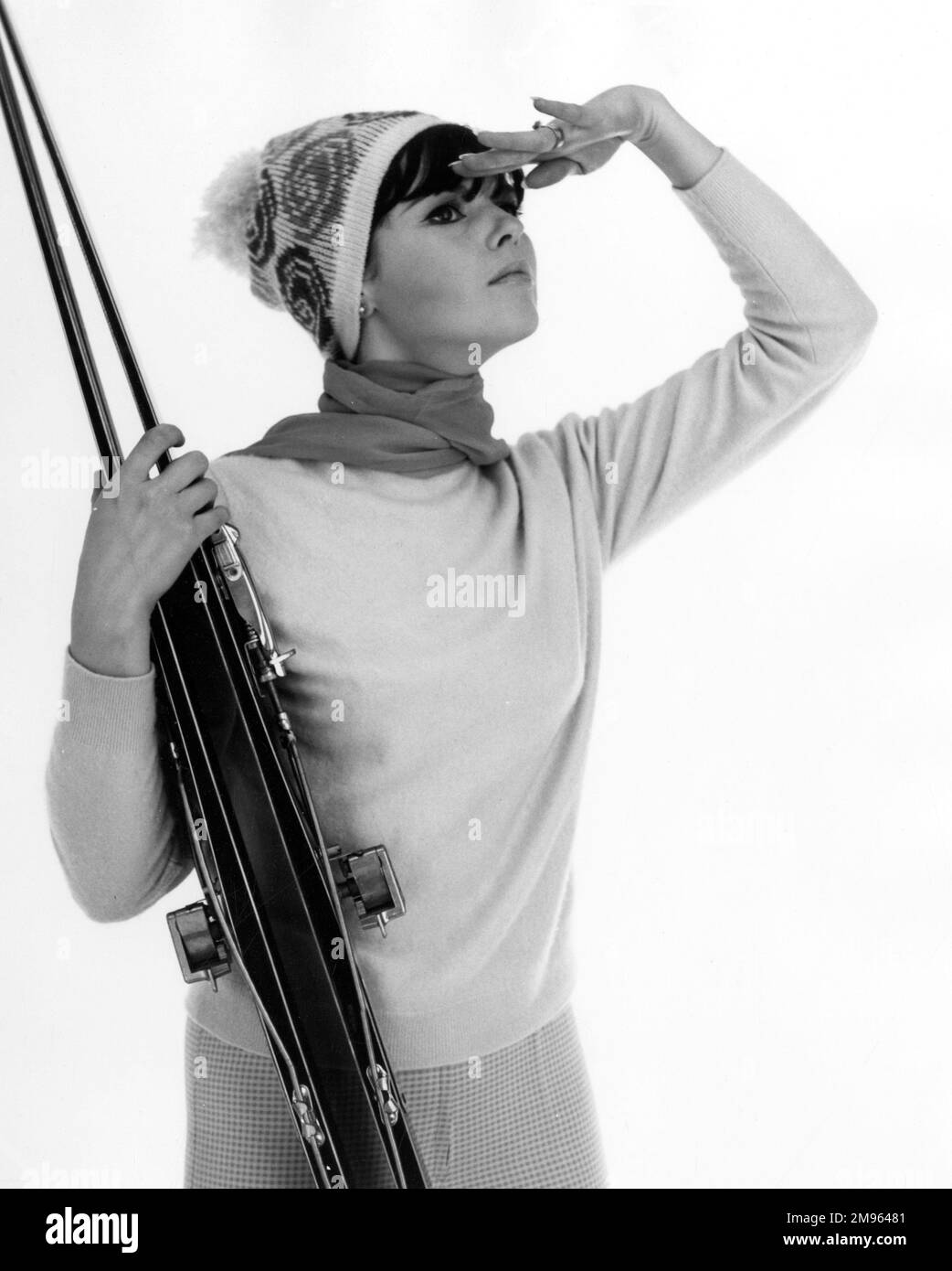Female model wearing a bobble hat and holding a pair of skis looking ...