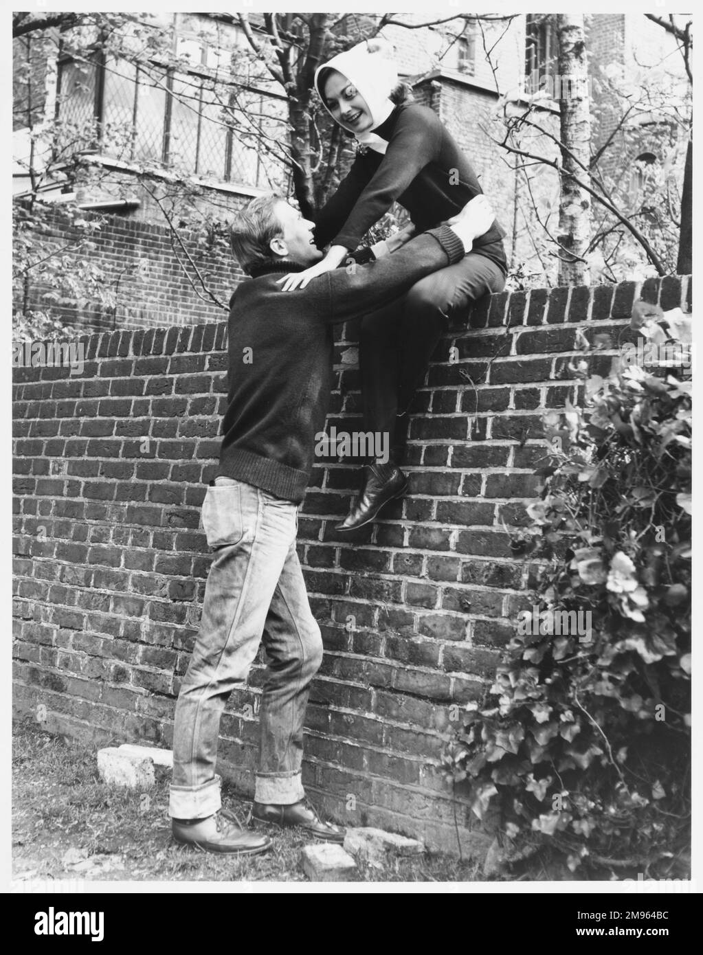 A man helps a woman up onto a wall Stock Photo - Alamy