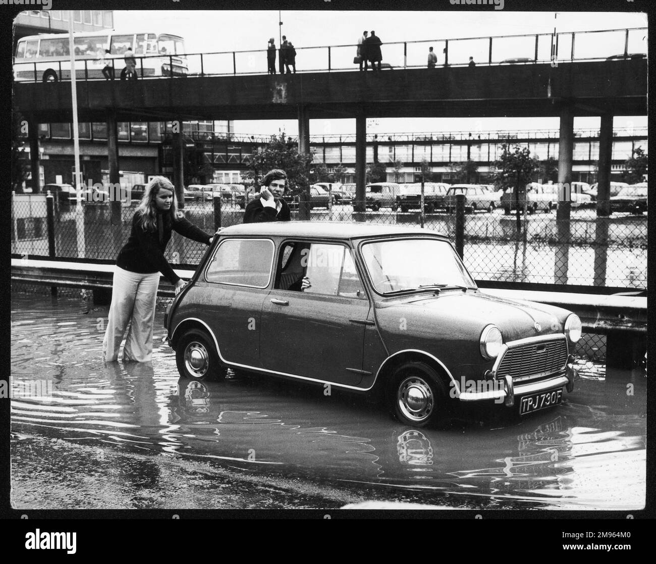 A young couple pushing their Mini car along the on the flooded A23 road ...