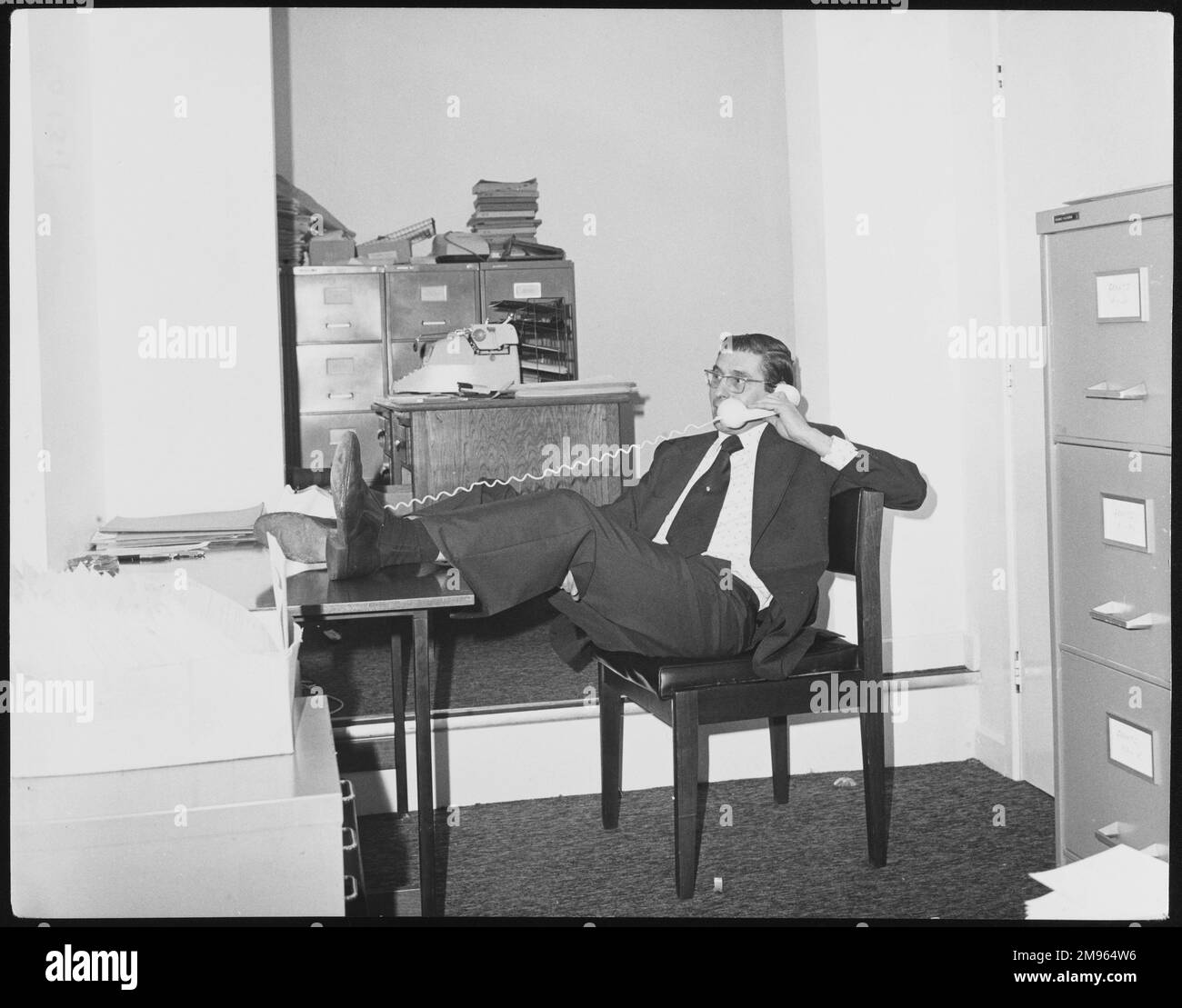 A businessman in a suit takes a phone call with his feet up on his desk ...