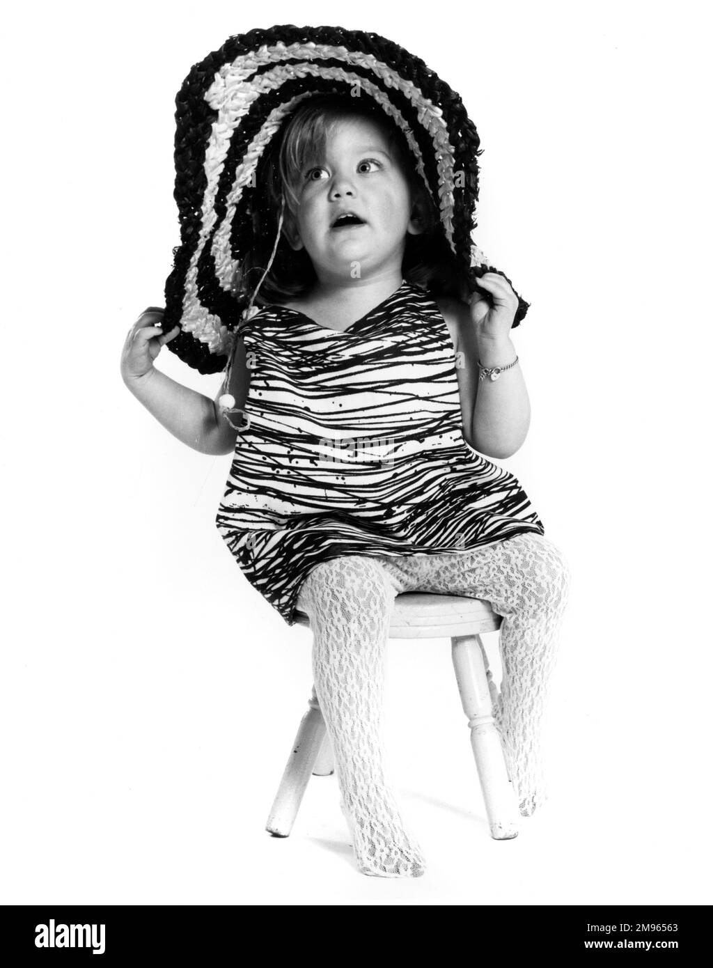 A little girl sitting on a stool wearing a fancy hat Stock Photo - Alamy