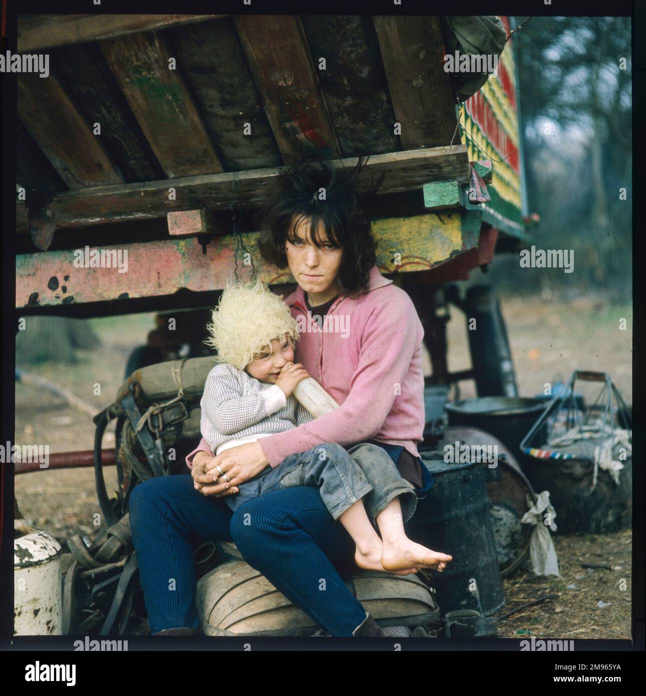 A rather sullen looking gypsy Mother and her child sit in the shade of ...