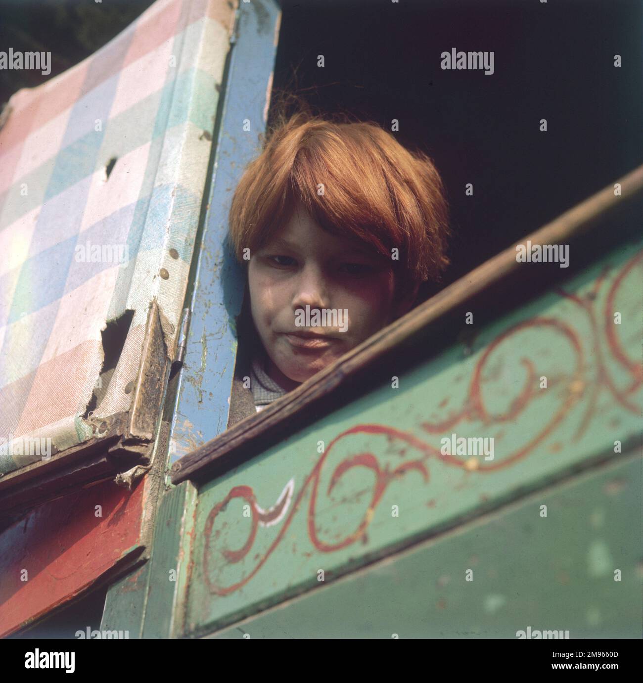 A young ginger-haired gypsy boy looks out from the window of the family ...