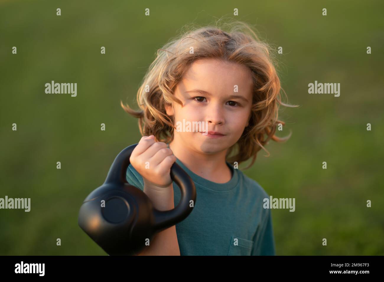 Child lifting the kettlebell in park outside. Child boy pumping up ...