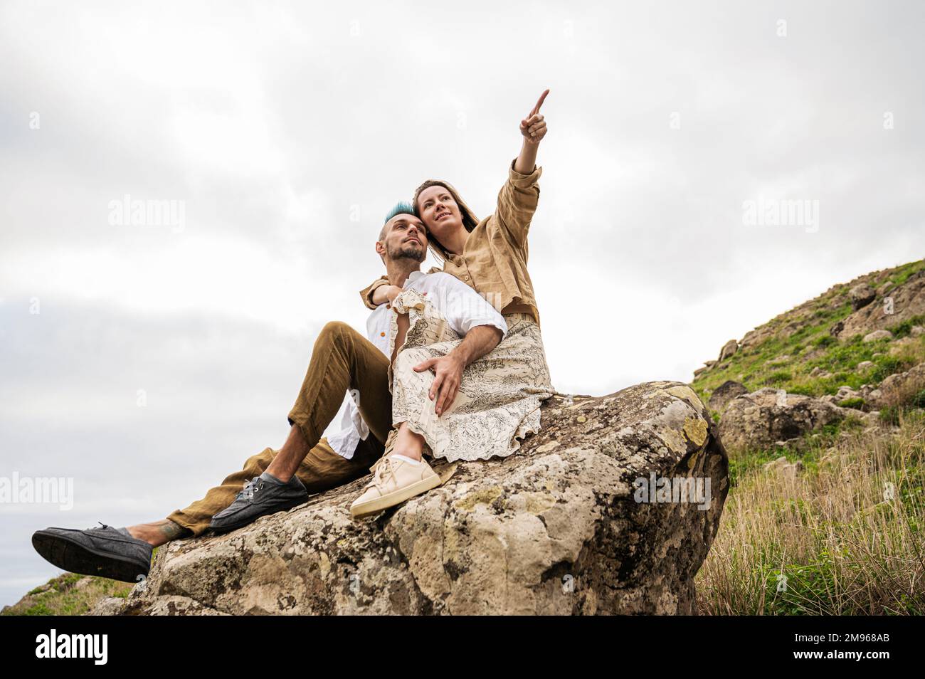 A young couple sits on a rock surrounded by hills and rocks in the ...