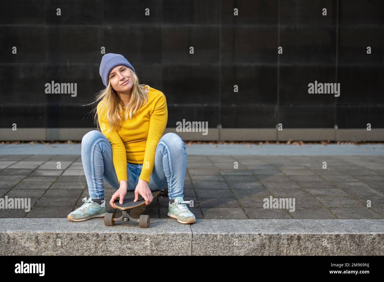 Young female teenager dressed in yellow jersey and jeans, sitting on a ...