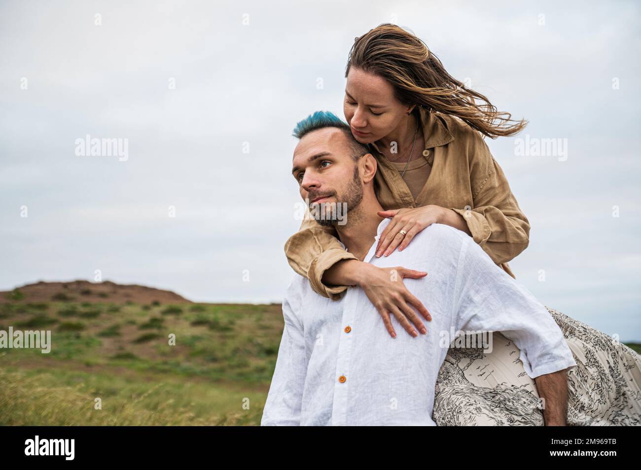 A young woman sits on a huge rock and embraces her partner from behind ...