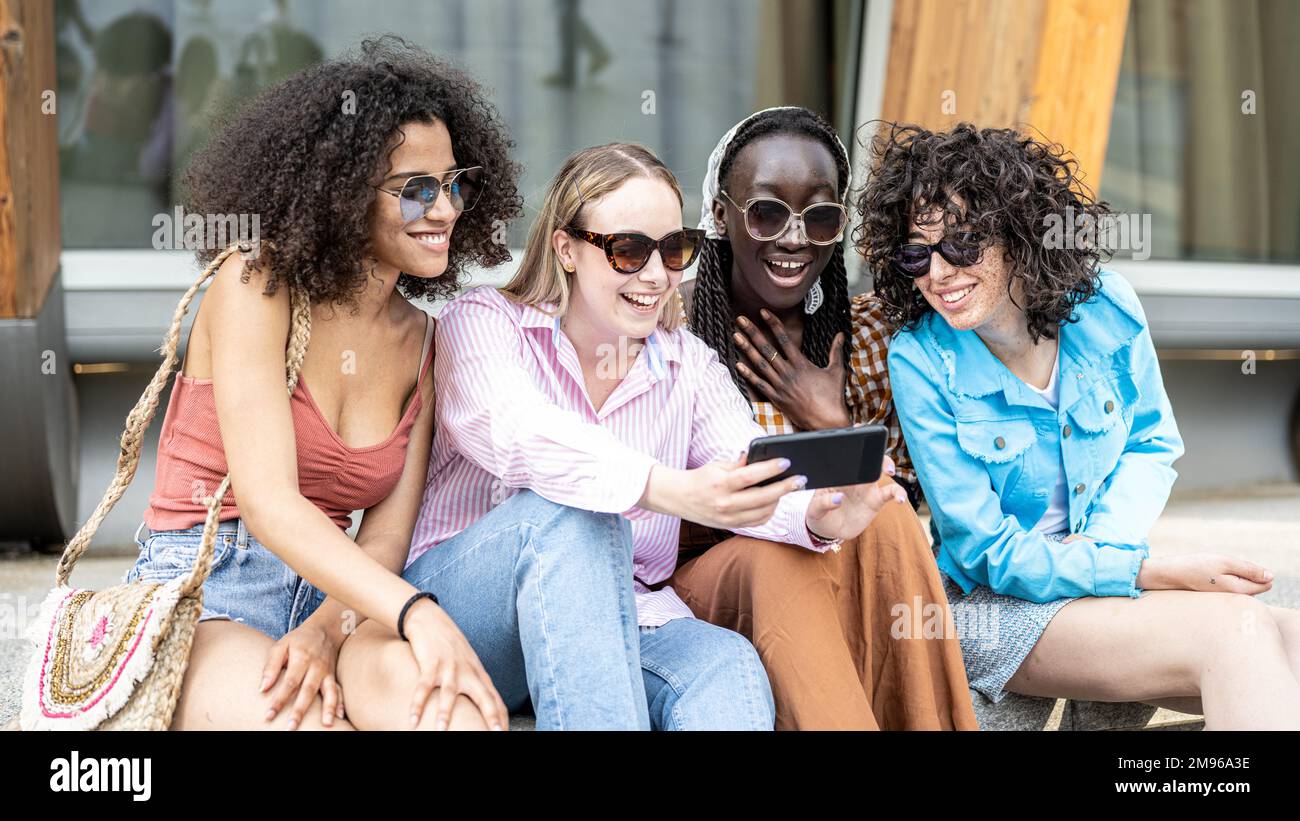 Four girls teenagers of Generation Z in the city, young women sitting ...