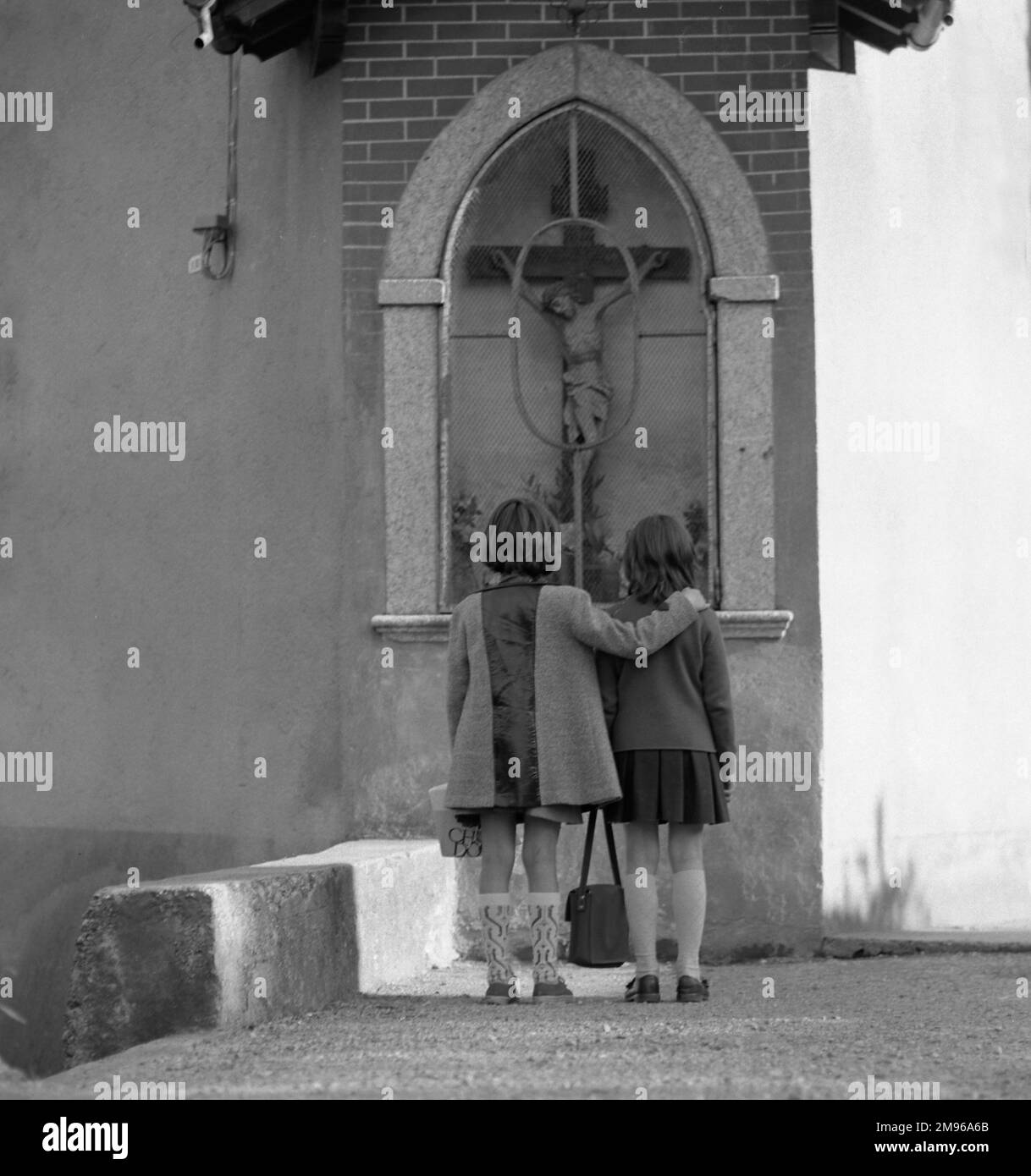 Two girls looking at a crucifix set in a gothic arch-shaped niche ...