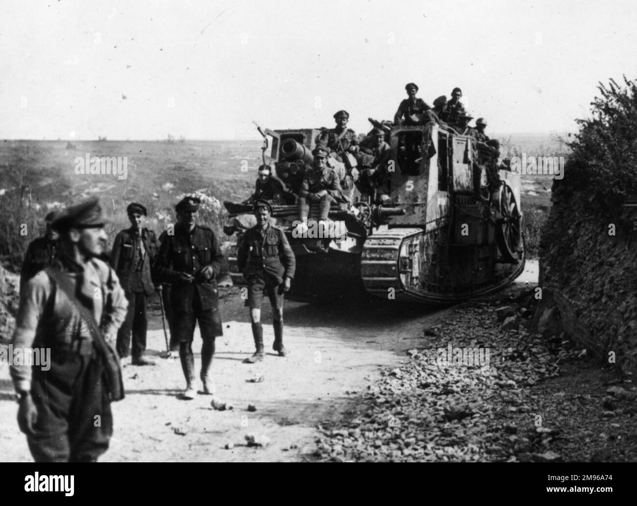 A group of soldiers marching along a road with a field gun on a tank ...