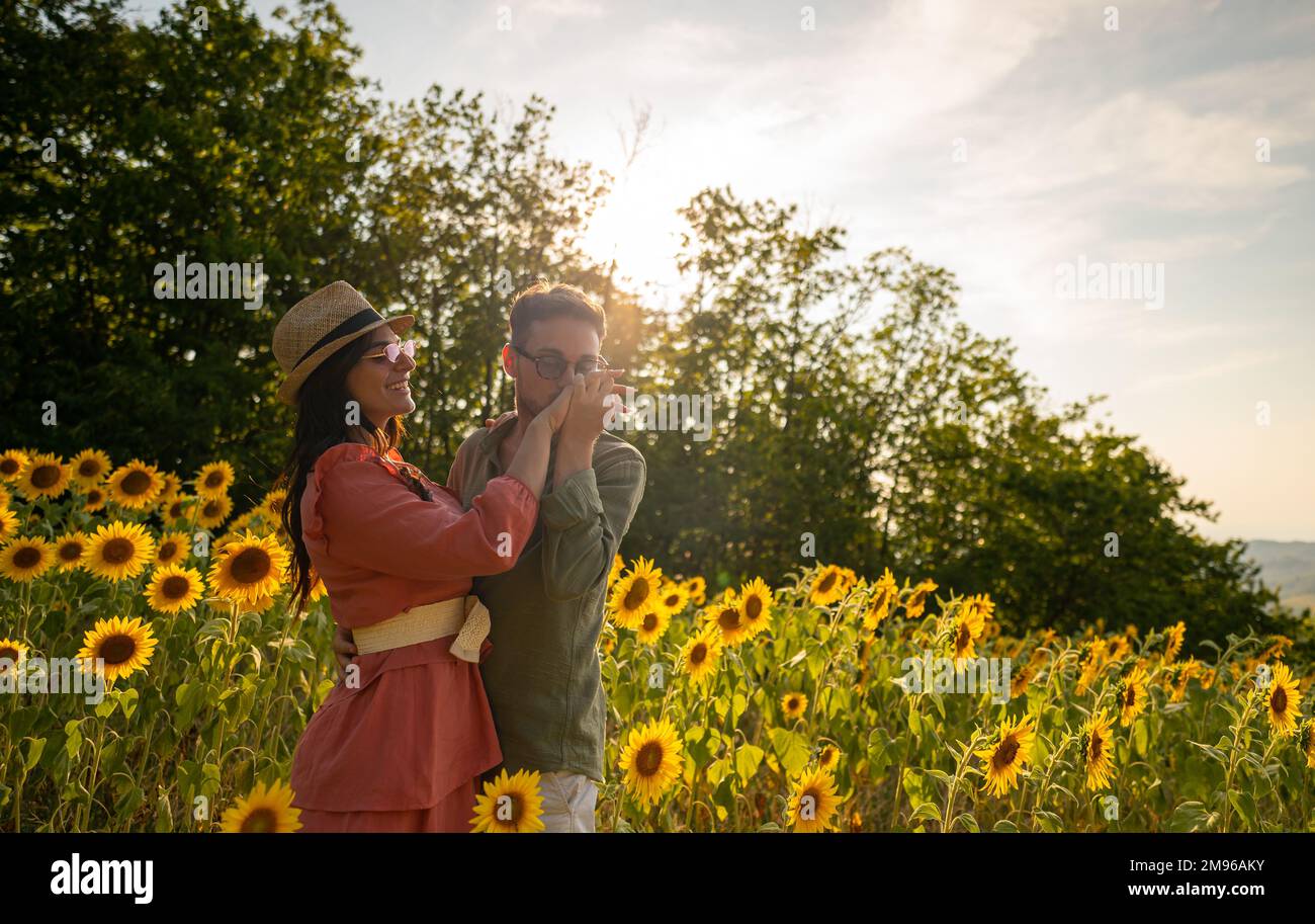 A young guy and his girlfriend stand in a field of sunflowers, romantic ...