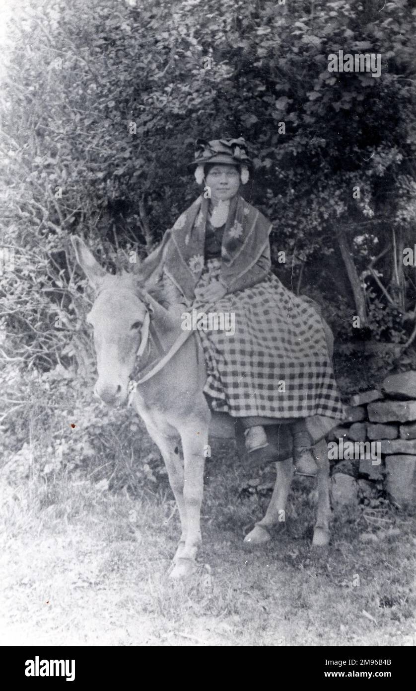 A young Welsh woman in traditional costume, riding a donkey sidesaddle ...