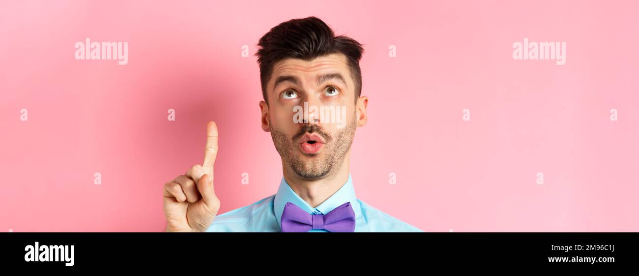 Intrigued young man in moustache, pointing finger and looking up at ...