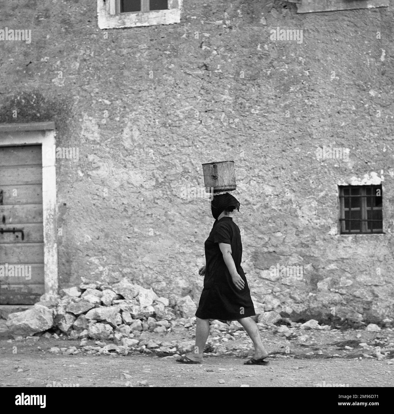 A woman in a black dress walks along a rubble-strewn street. She is ...