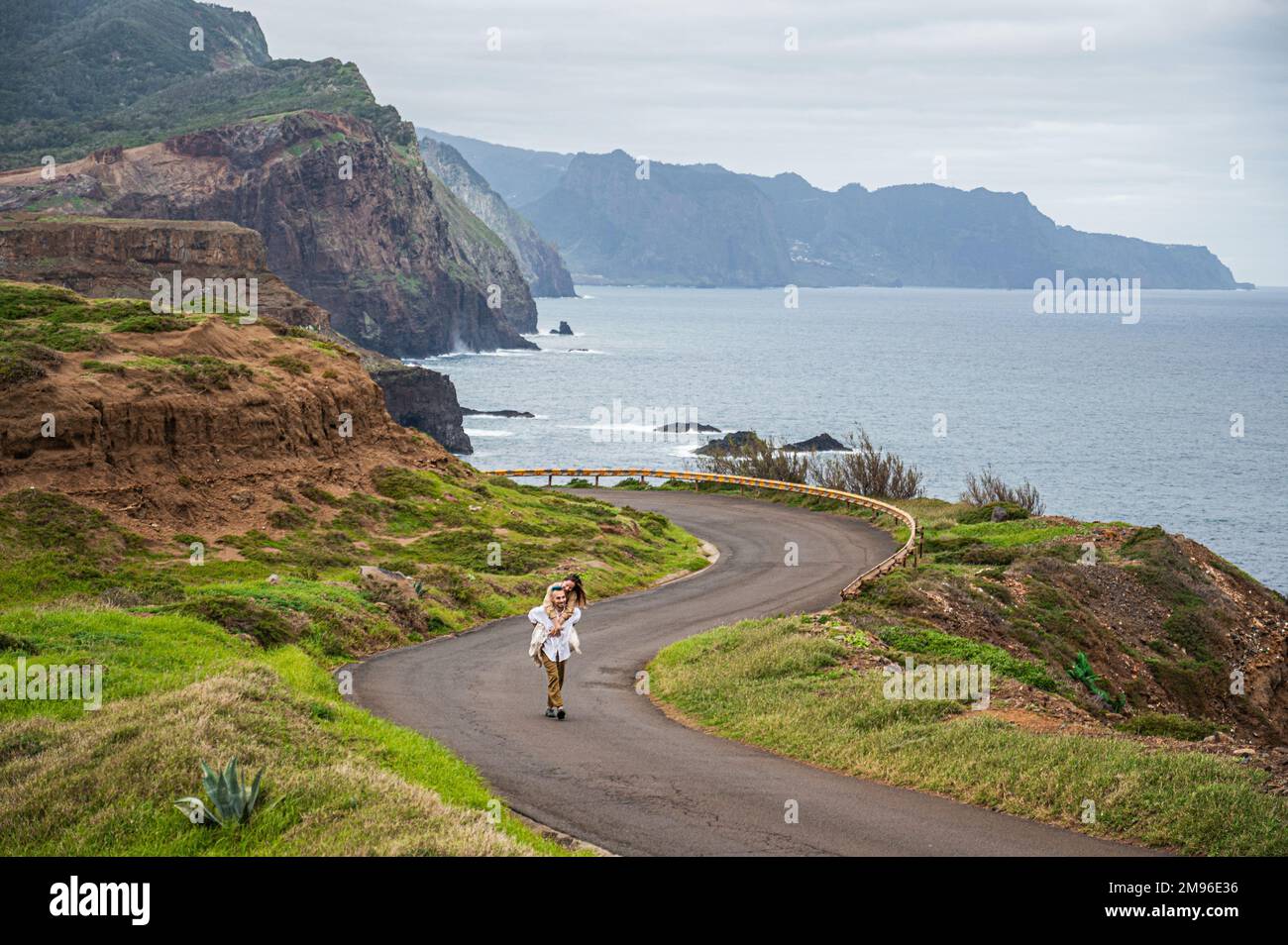 A distance shot of a young couple walking on a winding road, holding ...