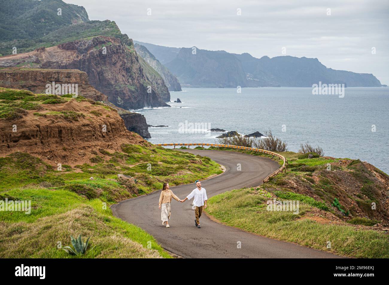 A distance shot of a young couple walking on a winding road, holding ...