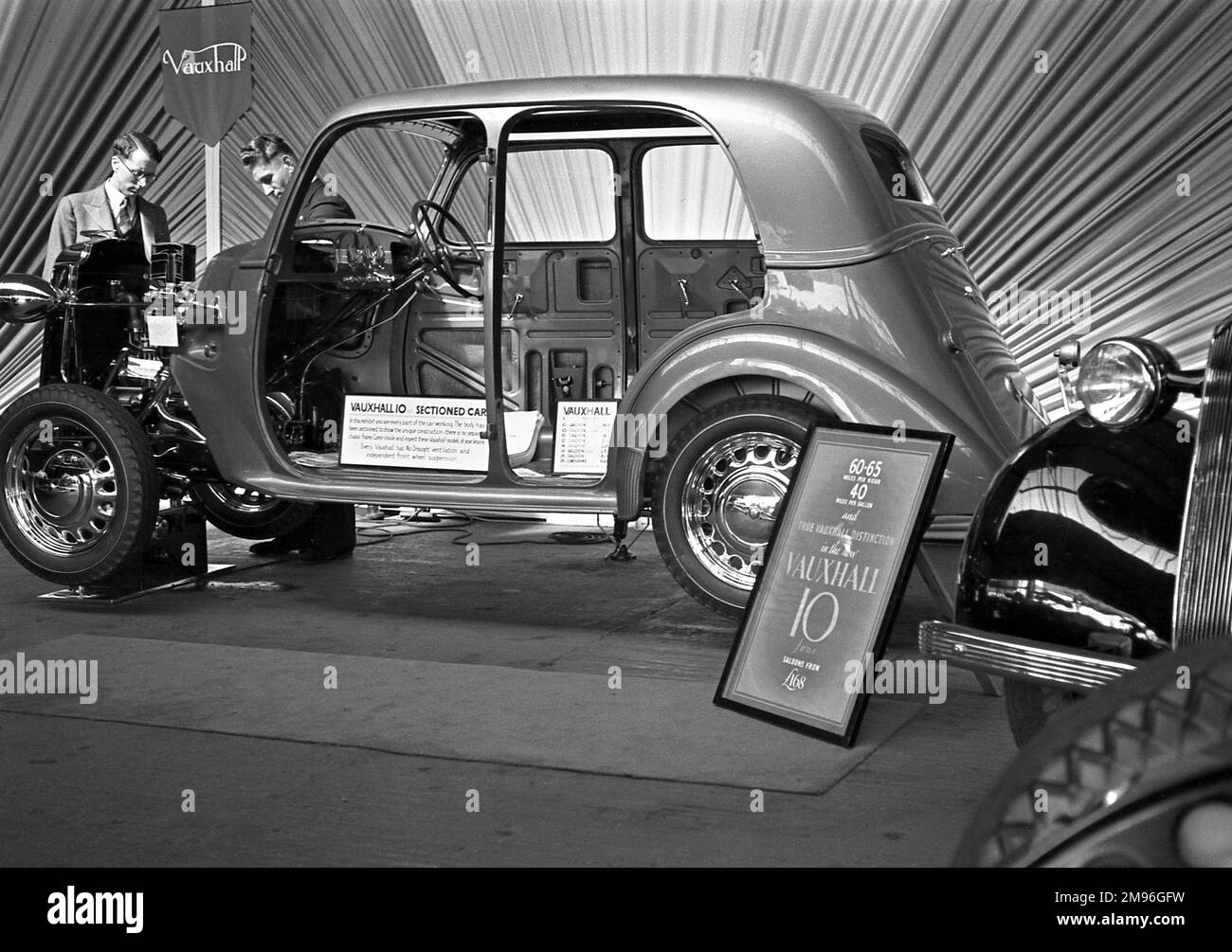 Scene in a car showroom, with a new Vauxhall 10 on display, stripped ...