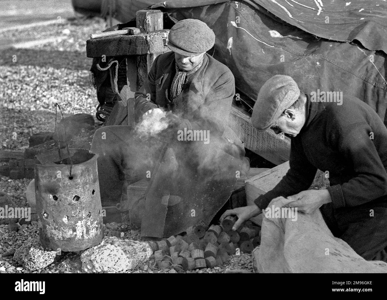 Two men sitting by a smoking brazier. The man on the right is putting ...