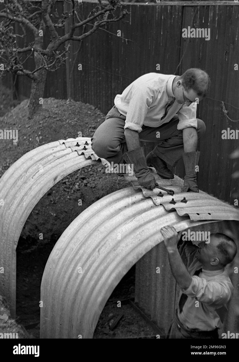 Two men constructing an Anderson shelter in a back garden at the start ...