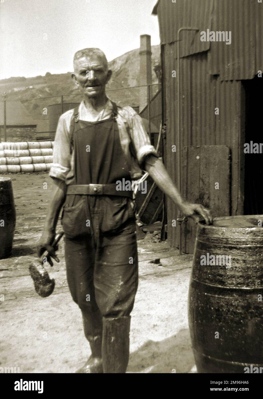 A middle-aged workman in overalls, standing next to a barrel Stock ...