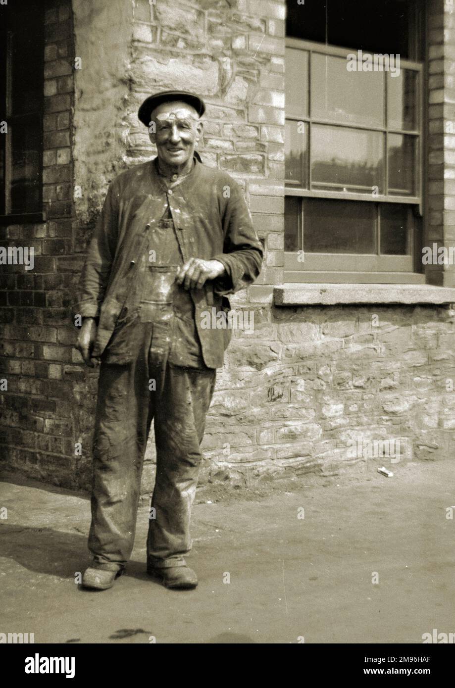 A middle-aged workman in dirty clothes, standing outside a building ...