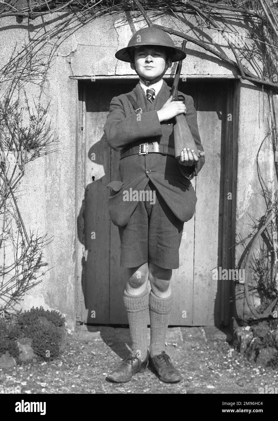 A boy in a tin helmet with a rifle on his shoulder, playing at being on ...