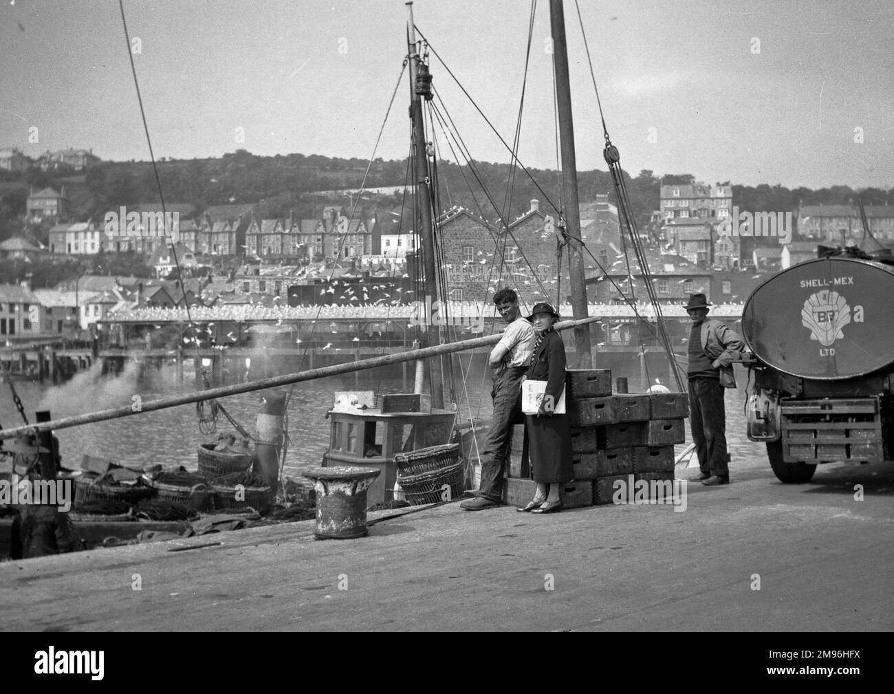 A harbour scene with fishing boats and seagulls. A Shell-Mex BP vehicle ...