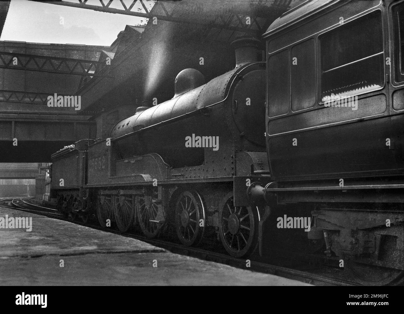 A steam engine with a passenger carriage attached, in a railway station ...